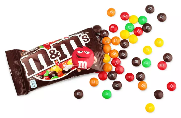 Apo ṣiṣi ti M&Ms lasan lori abẹlẹ funfun kan.